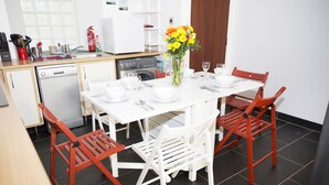 Cozinha moderna com máquina de lavar louça, máquina de lavar roupa e área de refeições com mesa branca posta para quatro pessoas.