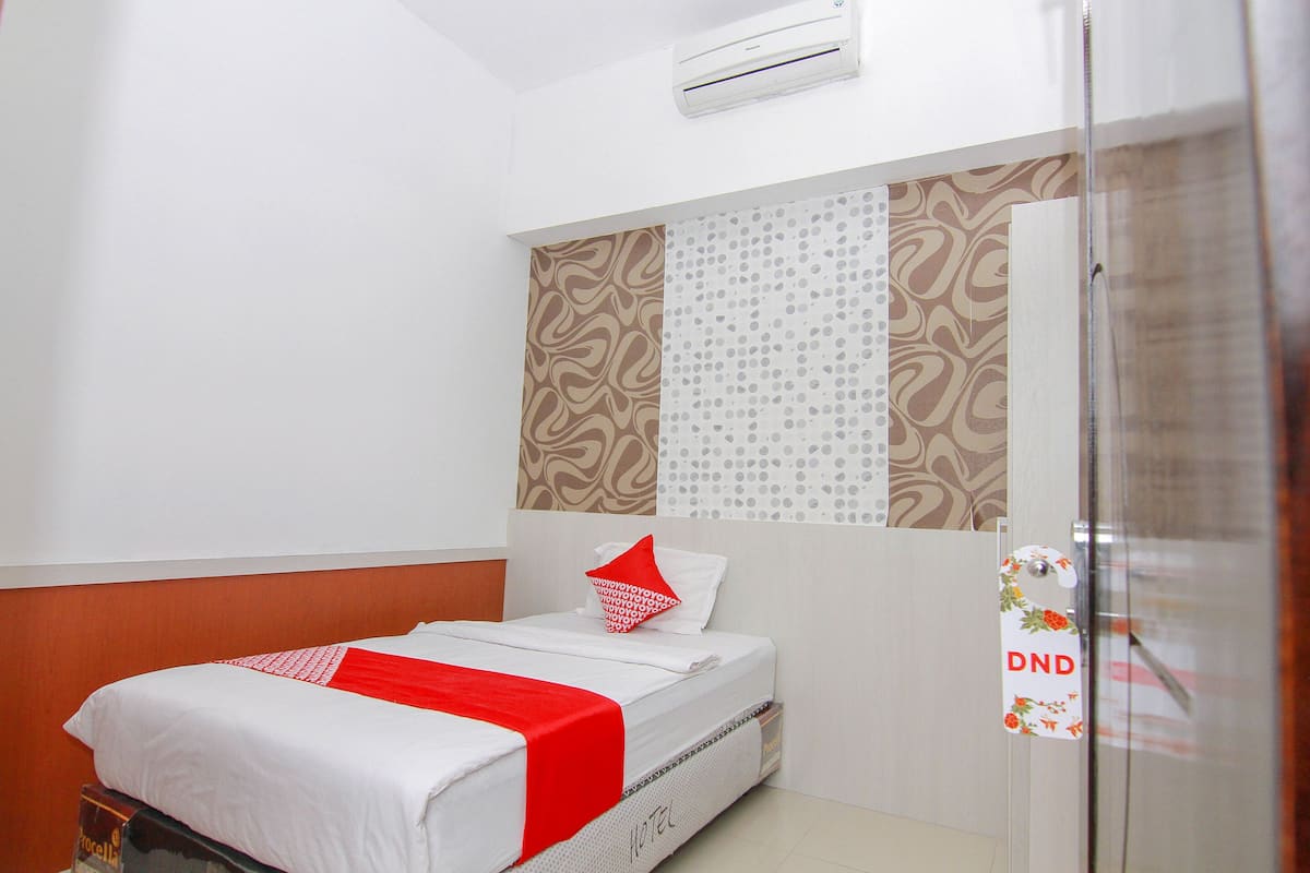 Quarto de hotel com cama, manta vermelha, cortinas estampadas e porta com placa de 'Não Perturbe'.