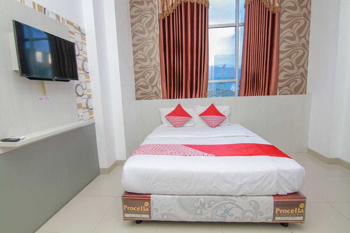 Quarto de hotel com cama, televisão de tela plana na parede e janela com cortinas.
