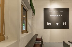 Interior de hotel com placa na parede indicando serviços como hotel, café e amor em Taitung. Há bancos ao longo da parede e uma janela com vista.