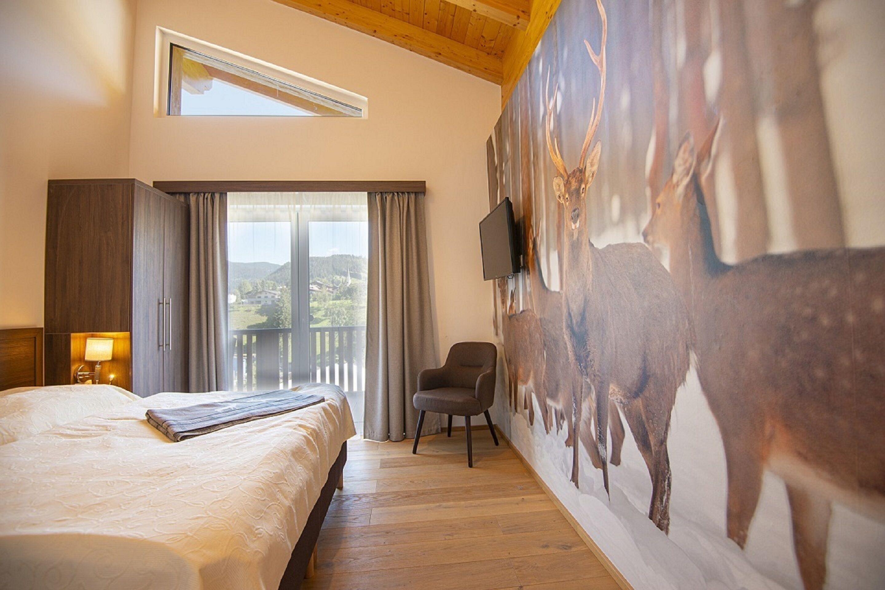 Quarto de hotel com uma cama grande, uma cadeira, uma TV fixada na parede e uma vista panorâmica pela janela.
