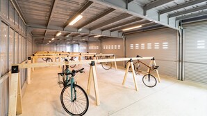 Amplo espaço interno com várias bicicletas estacionadas nas paredes, suportes de madeira para bicicletas e uma grande porta de garagem.