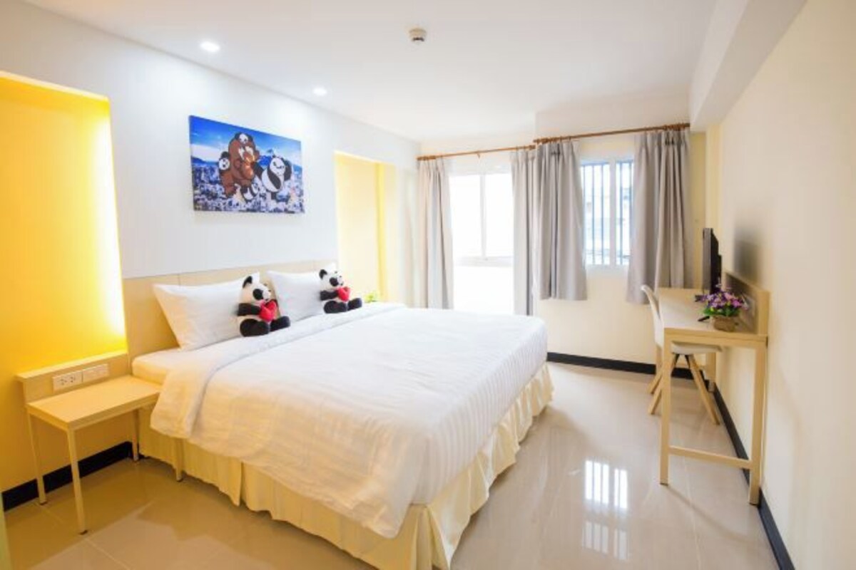 Quarto de hotel com uma cama grande, mesas de cabeceira, uma escrivaninha com cadeira, televisão e um quadro na parede.