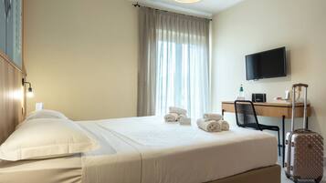 Quarto de hotel com cama, escrivaninha, cadeira, televisão e mala.