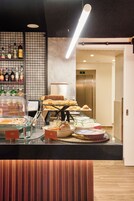 Uma área de buffet com diversos alimentos, um expositor de vidro e uma parede com garrafas.