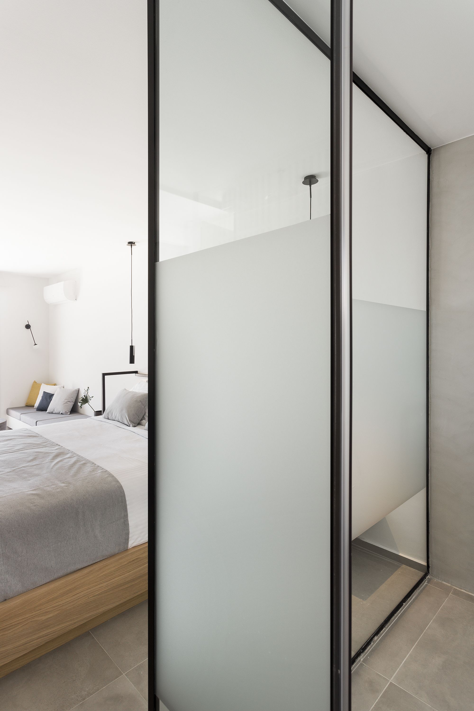 Quarto moderno com cama, mesa de cabeceira, abajur e porta de vidro deslizante.