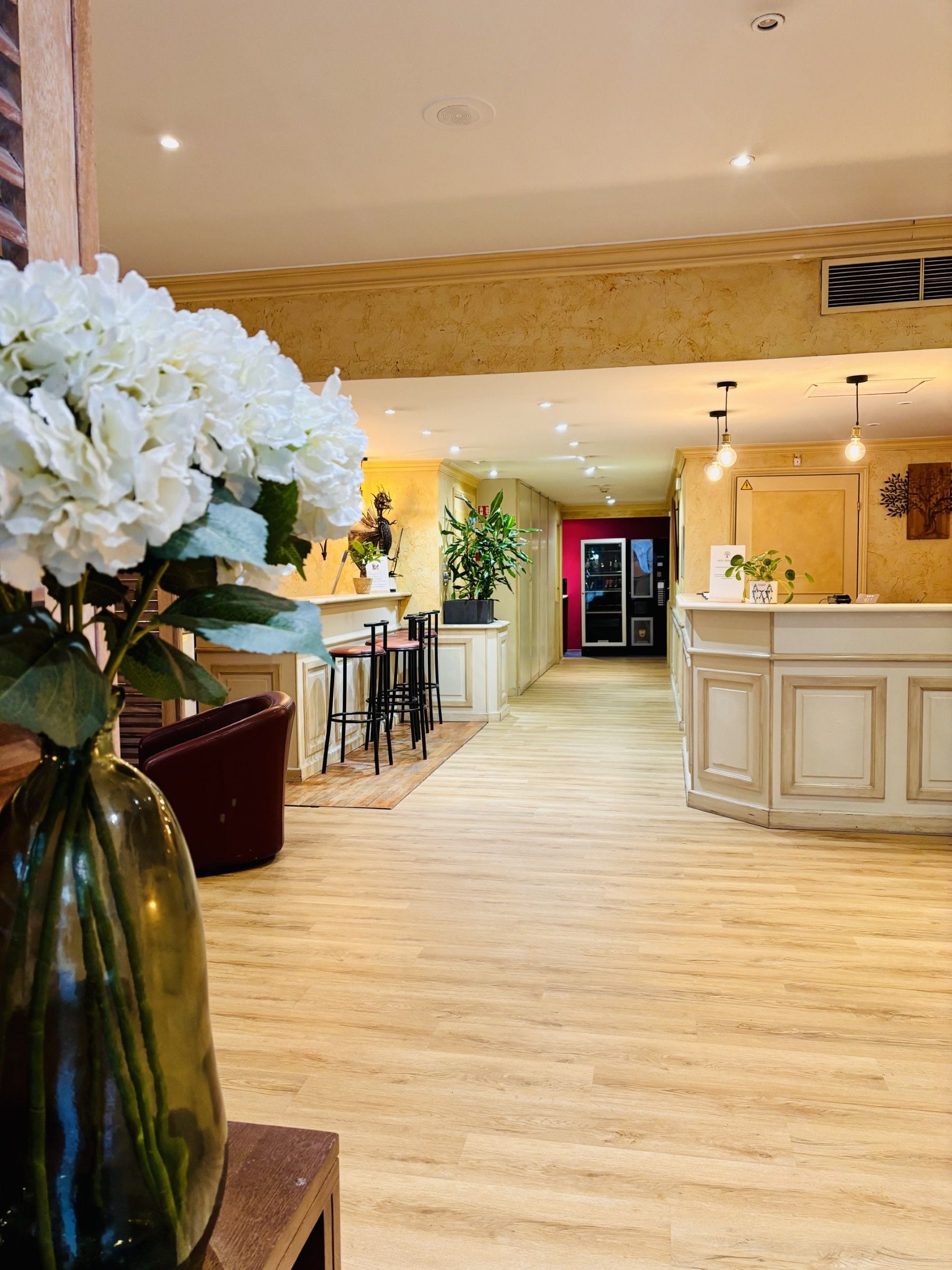 Um saguão de hotel com piso de madeira, balcão de recepção e área de estar com cadeiras e uma mesa.