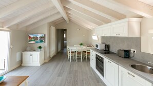 Uma cozinha espaçosa com armários brancos, um espaço de jantar com mesa e cadeiras, e vista para a sala adjacente.