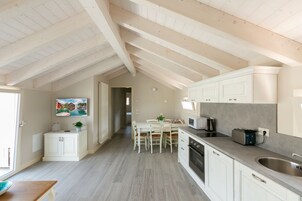 Uma cozinha espaçosa com armários brancos, um espaço de jantar com mesa e cadeiras, e vista para a sala adjacente.