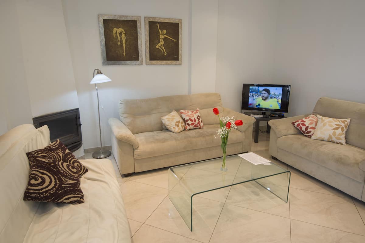 Uma sala de estar com dois sofás, uma mesa de centro de vidro, uma televisão e um abajur.