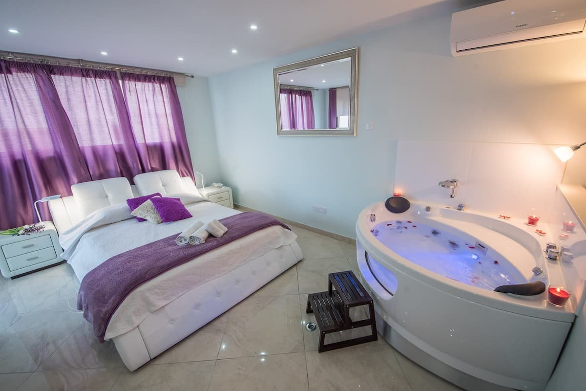 Quarto moderno com cama grande, área de estar, banheira e espelho.