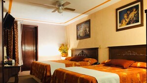 Quarto de hotel com duas camas, um ventilador de teto, um quadro e uma escrivaninha com abajur.