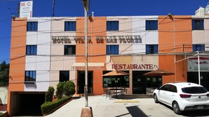 Um edifício de vários andares com a placa 'Hotel Villa de las Flores' e um restaurante.