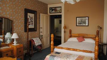 Um quarto com uma cama de madeira baldaquino, uma mesa de cabeceira com luminárias, um aparador e uma porta que dá para outro cômodo.
