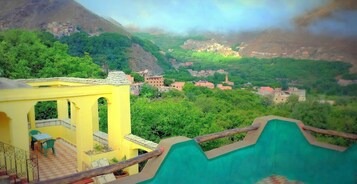 Um edifício amarelo com varanda, com vista para um vale com casas e vegetação.