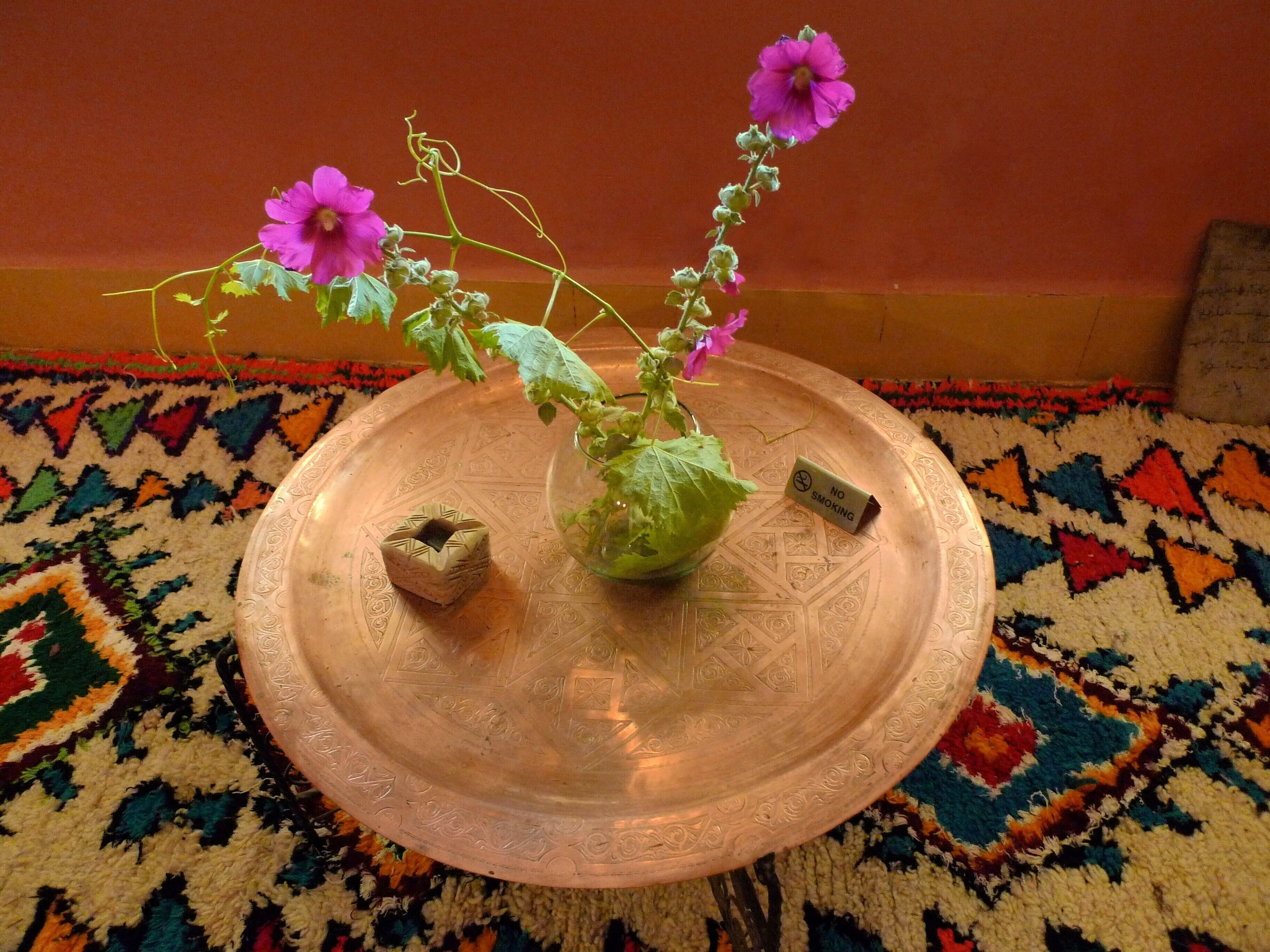 Uma bandeja de cobre com um vaso de vidro contendo flores cor-de-rosa e uma pequena pedra.