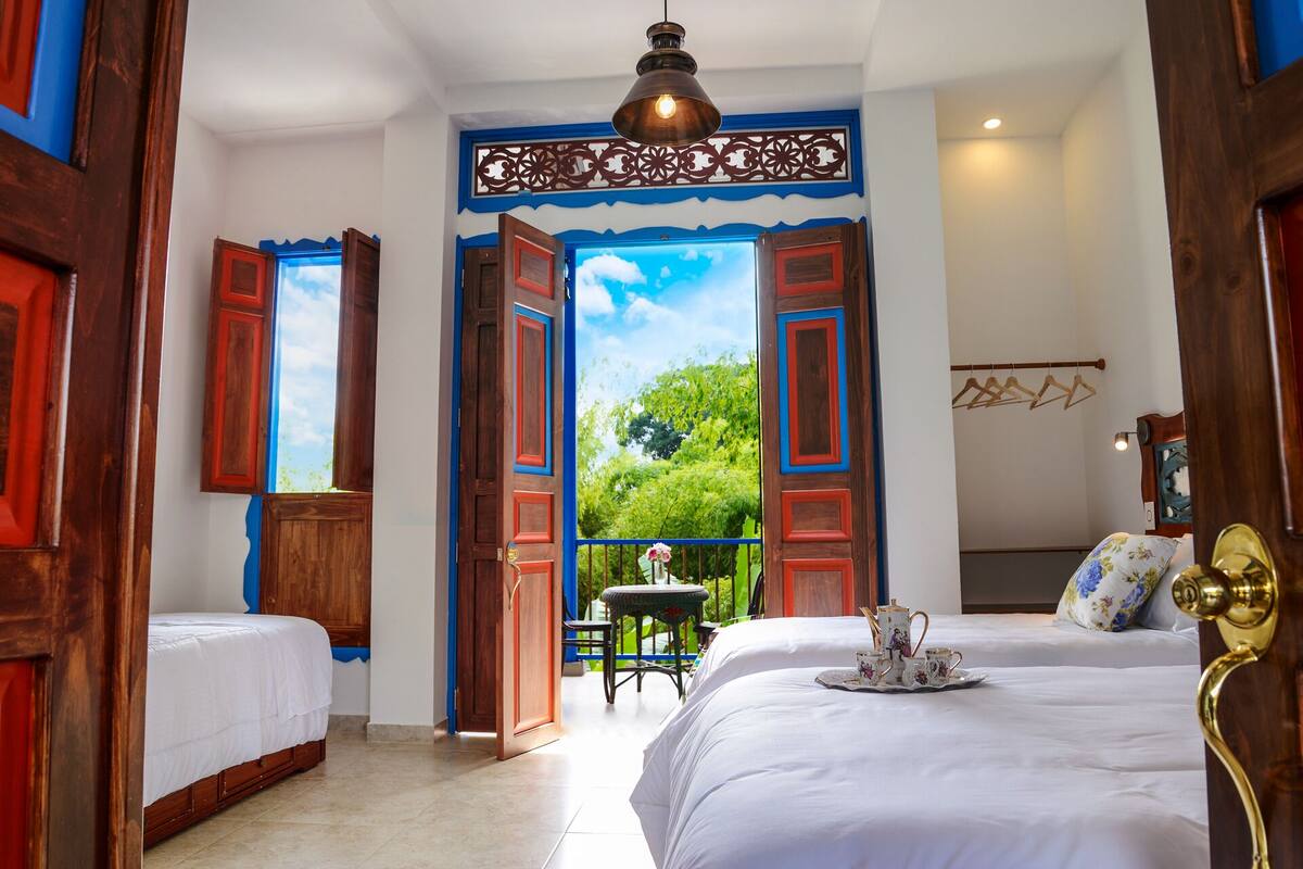 Quarto de hotel com duas camas, varanda e vista, e luminária pendente.