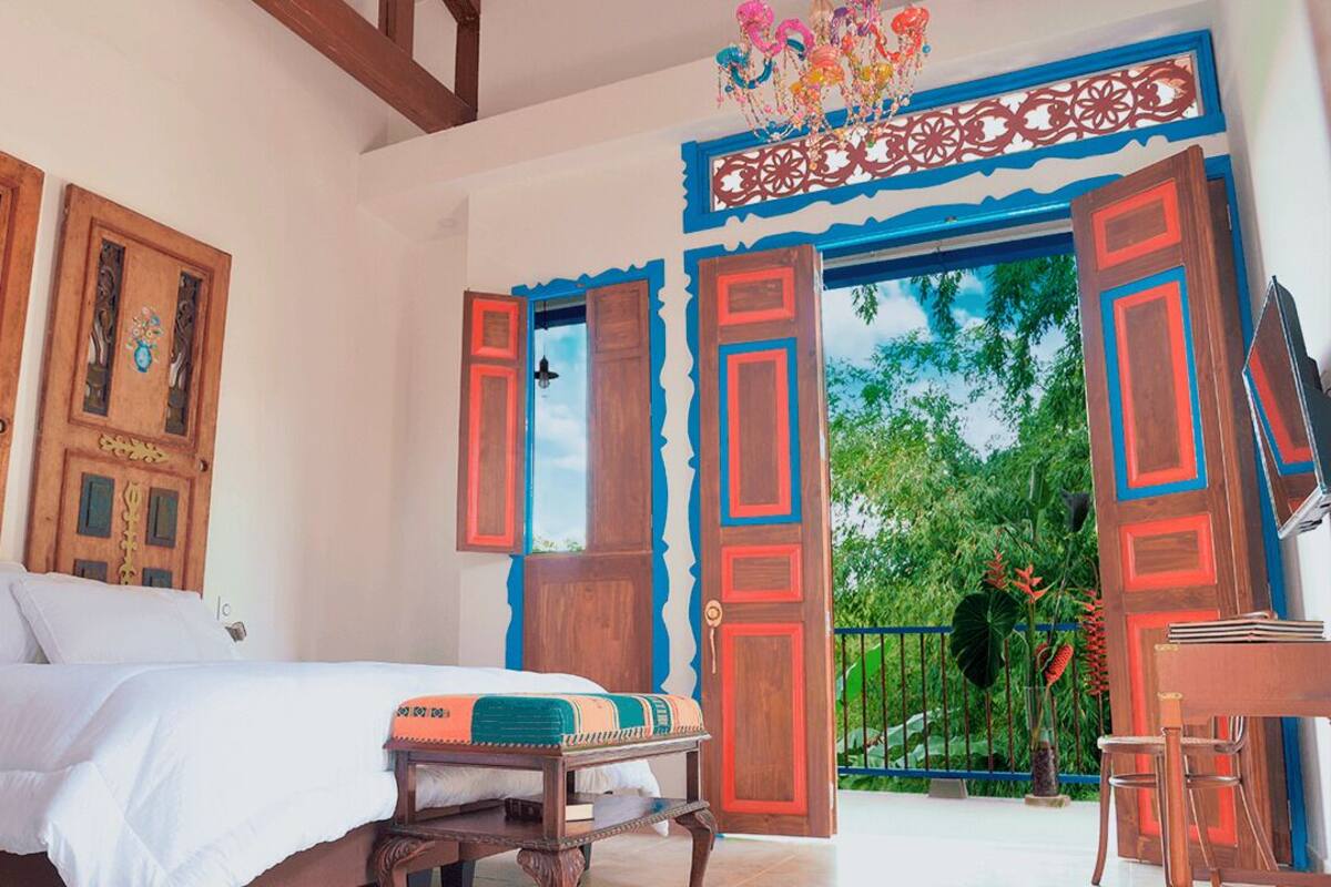 Quarto com cama, um banco de madeira e vista para o exterior através de uma porta.