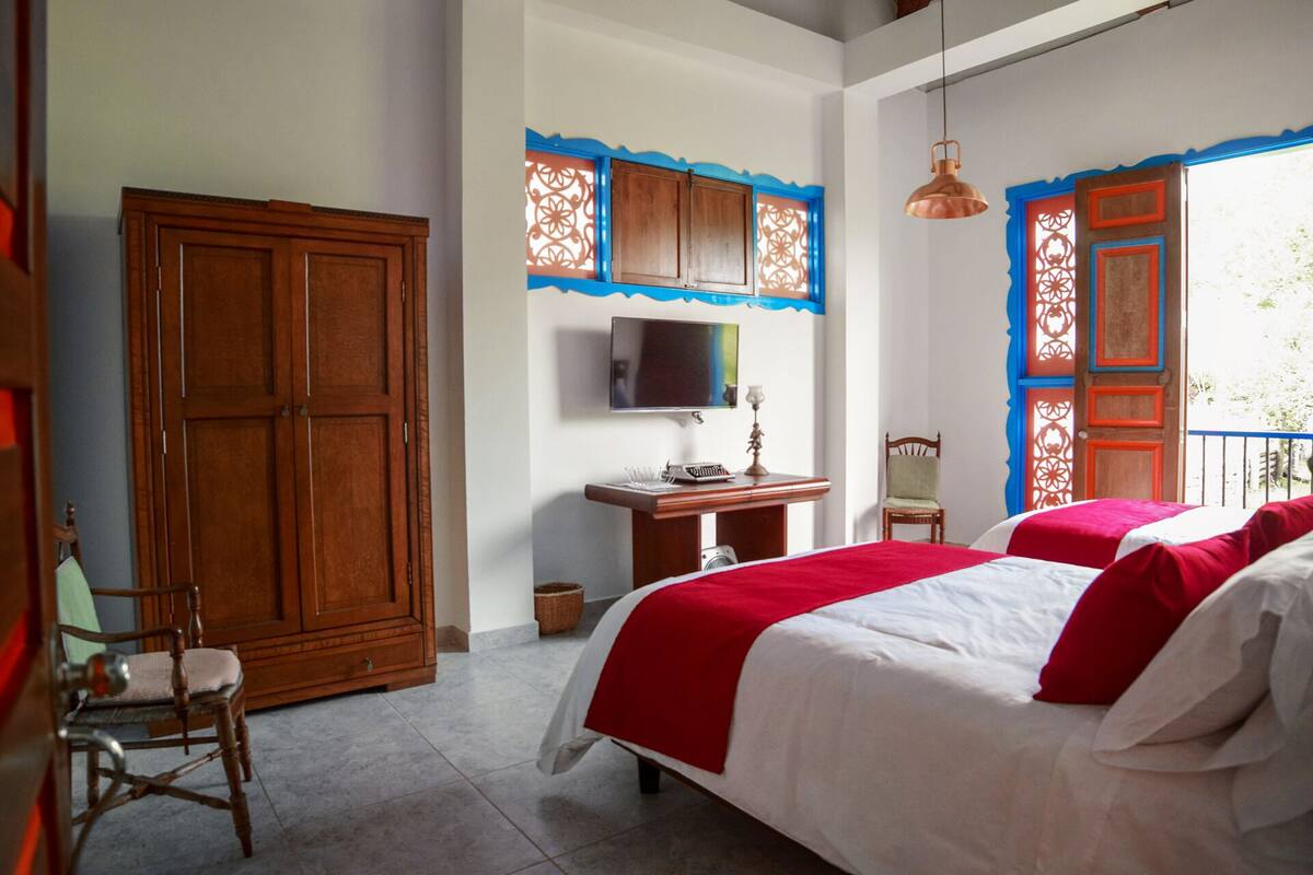 Quarto com cama, escrivaninha, televisão, guarda-roupa e uma cadeira.