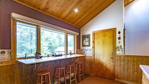 Uma cozinha com banquetas de madeira, uma janela com vista para árvores e uma porta decorada com tema de jardim.