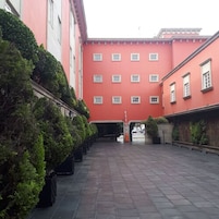 Um pátio com um edifício vermelho, portão e arbustos bem aparados.