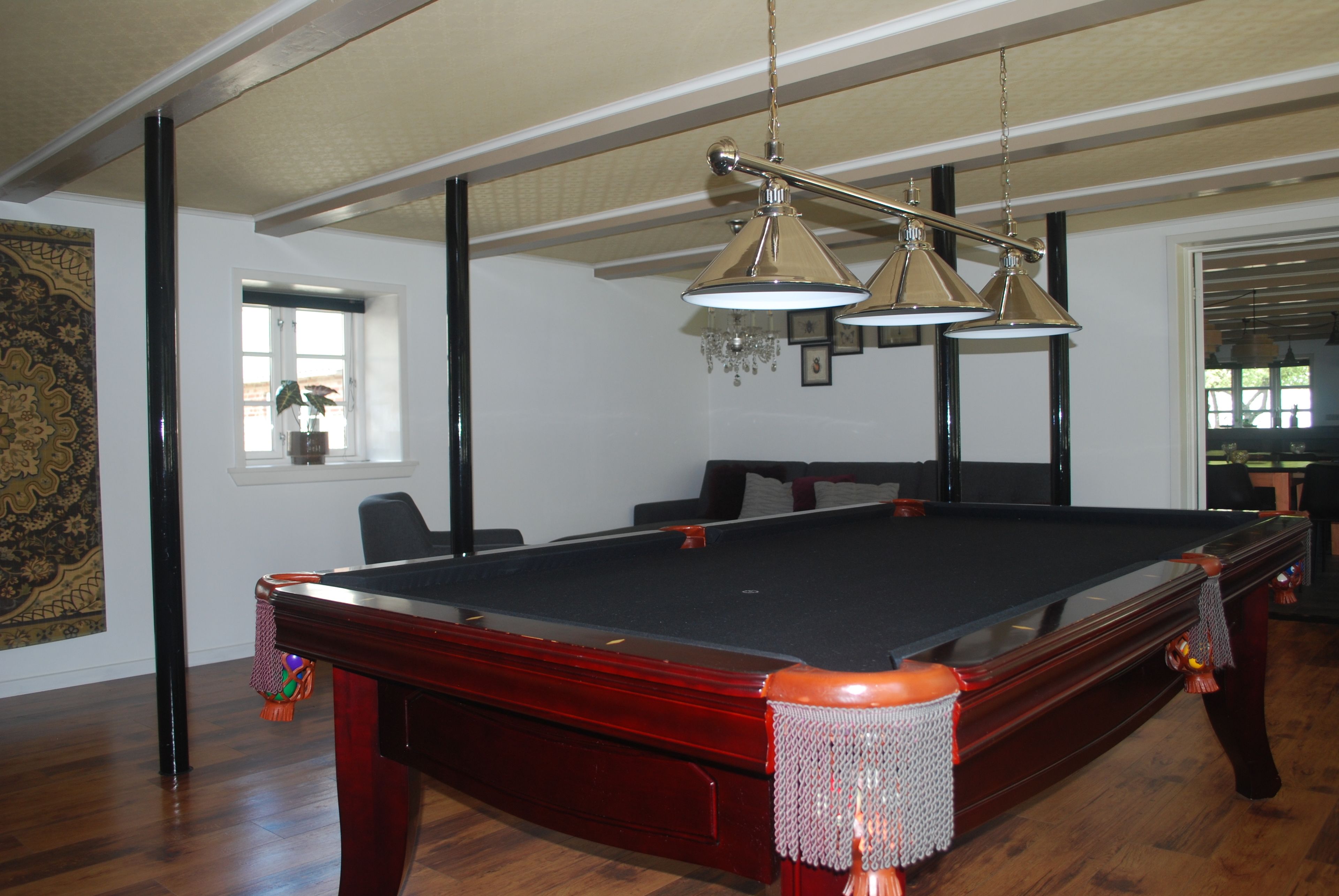 Uma mesa de bilhar em um espaço com piso de madeira, um candelabro e uma janela com vista.