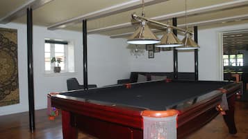 Uma mesa de bilhar em um espaço com piso de madeira, um candelabro e uma janela com vista.