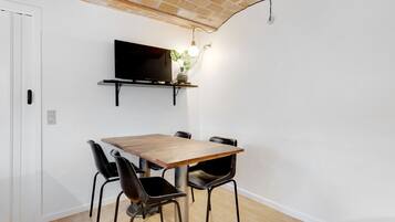 Uma área de refeições com uma mesa de madeira e quatro cadeiras, uma TV de tela plana na parede e um lustre.