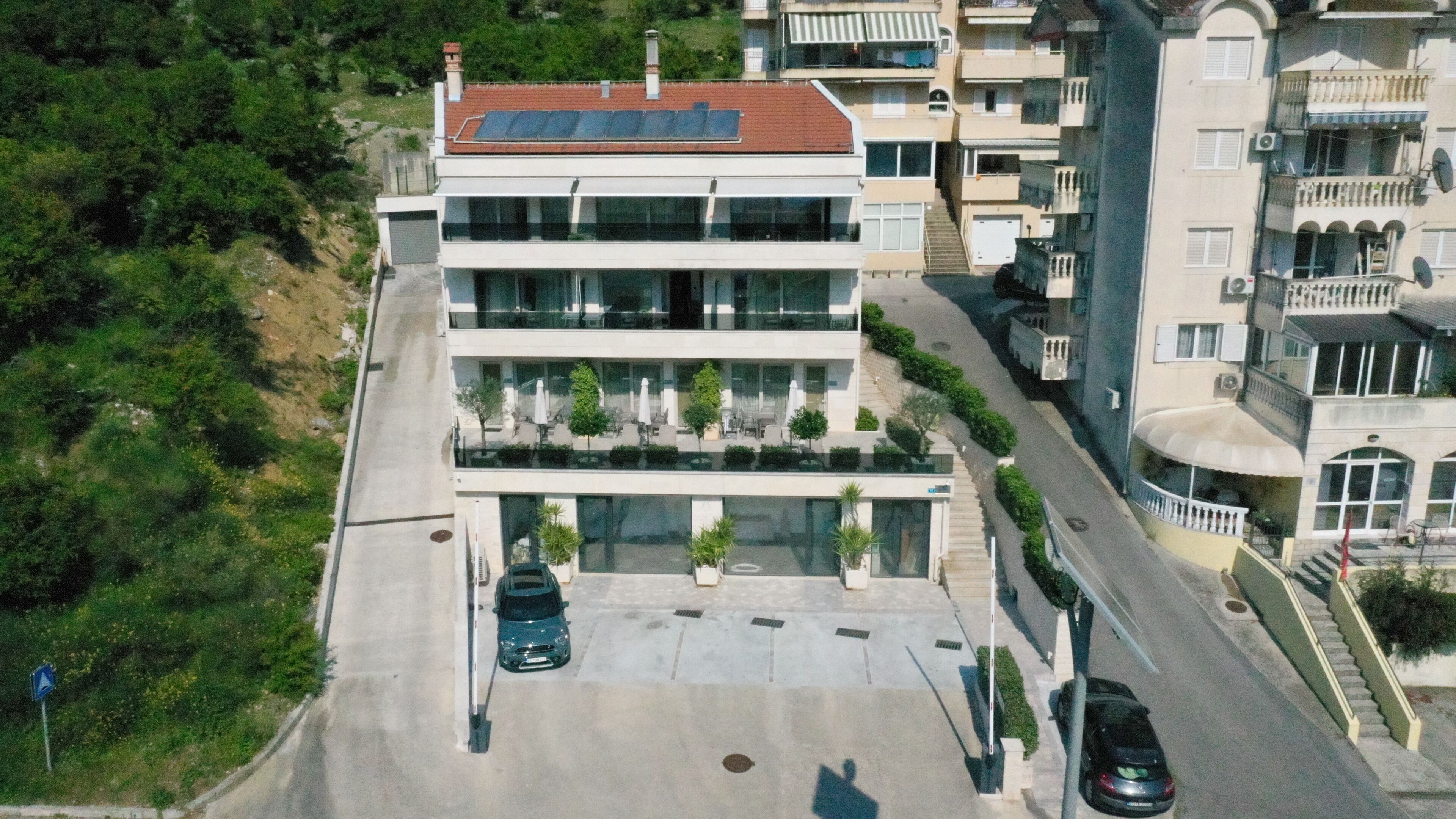 Um edifício com vários andares, telhado plano, amplas janelas e estacionamento com carros.