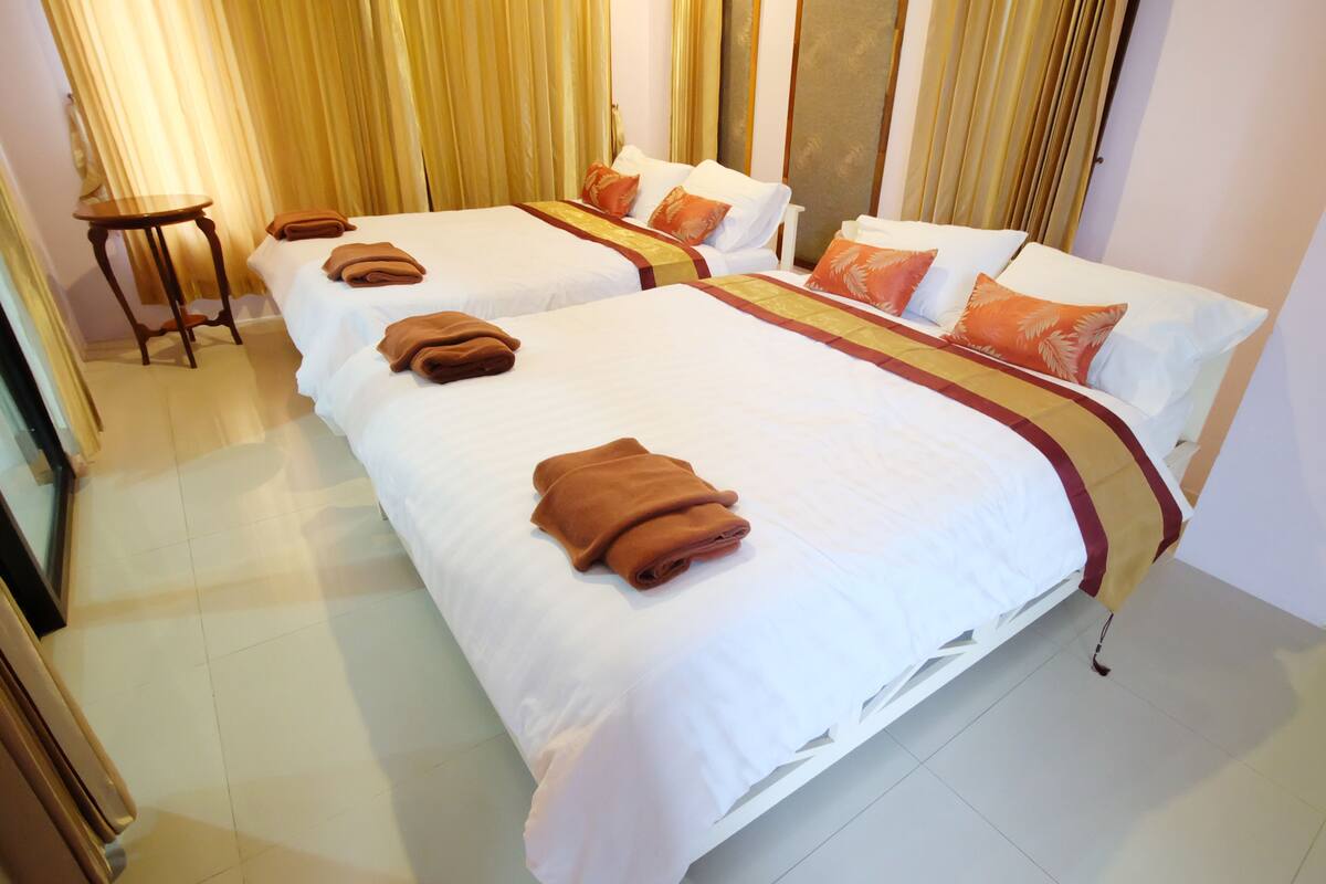Quarto de hotel com duas camas, cada uma com roupa de cama branca e toalhas castanhas. Há uma pequena mesa e um espelho no canto.