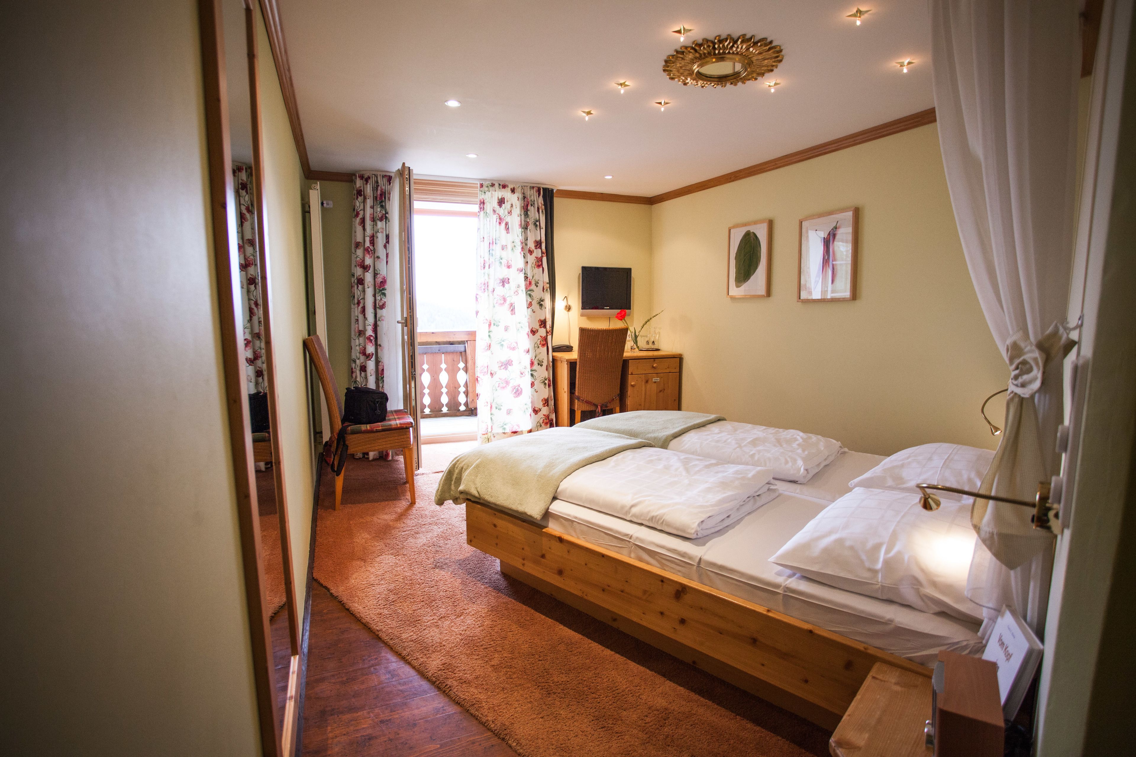 Quarto com cama de madeira, escrivaninha com cadeira, televisão e mesa pequena.