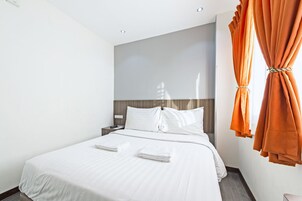 Quarto de hotel com uma cama grande, roupa de cama branca, cabeceira de madeira e cortinas laranja.
