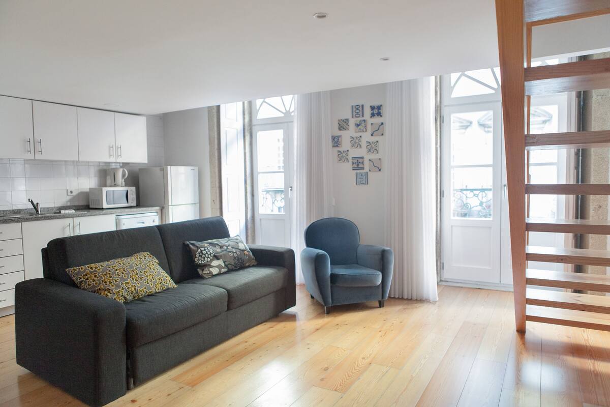 Uma sala de estar moderna com um sofá cinza, uma poltrona azul e piso de madeira.