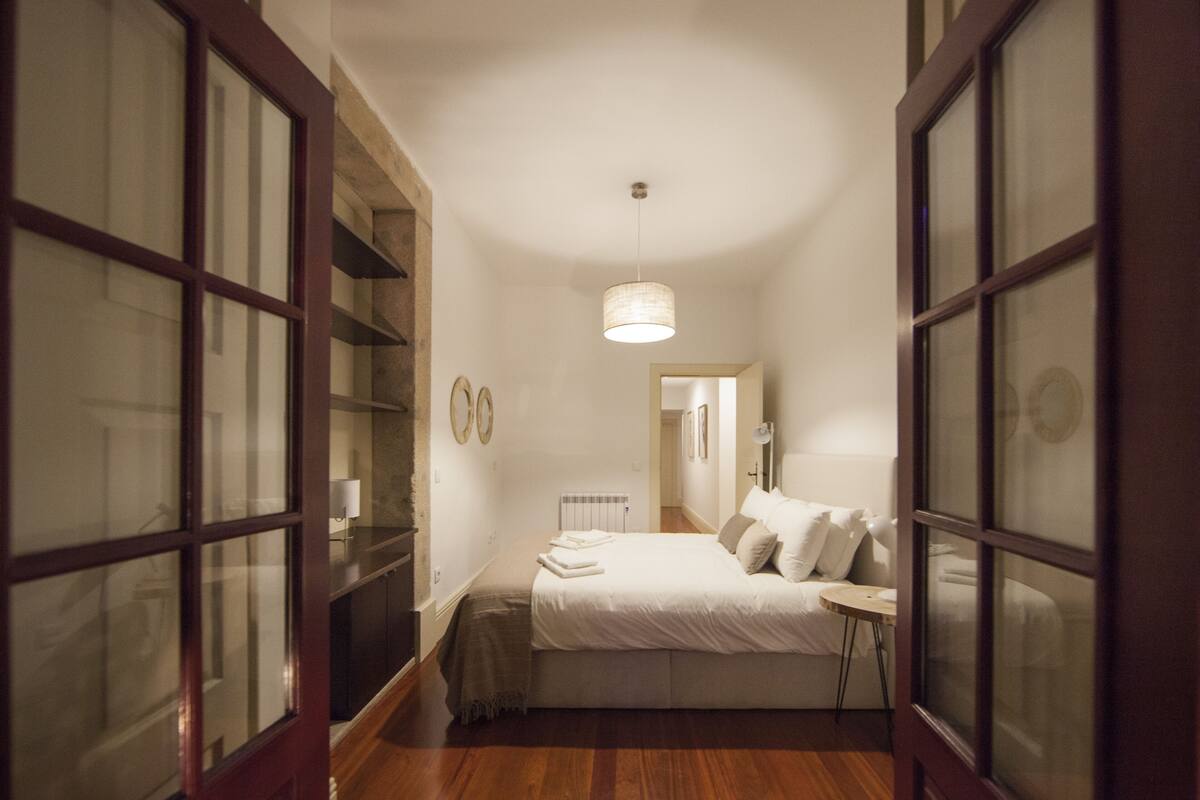 Um quarto pequeno com uma cama, uma mesinha e um radiador.