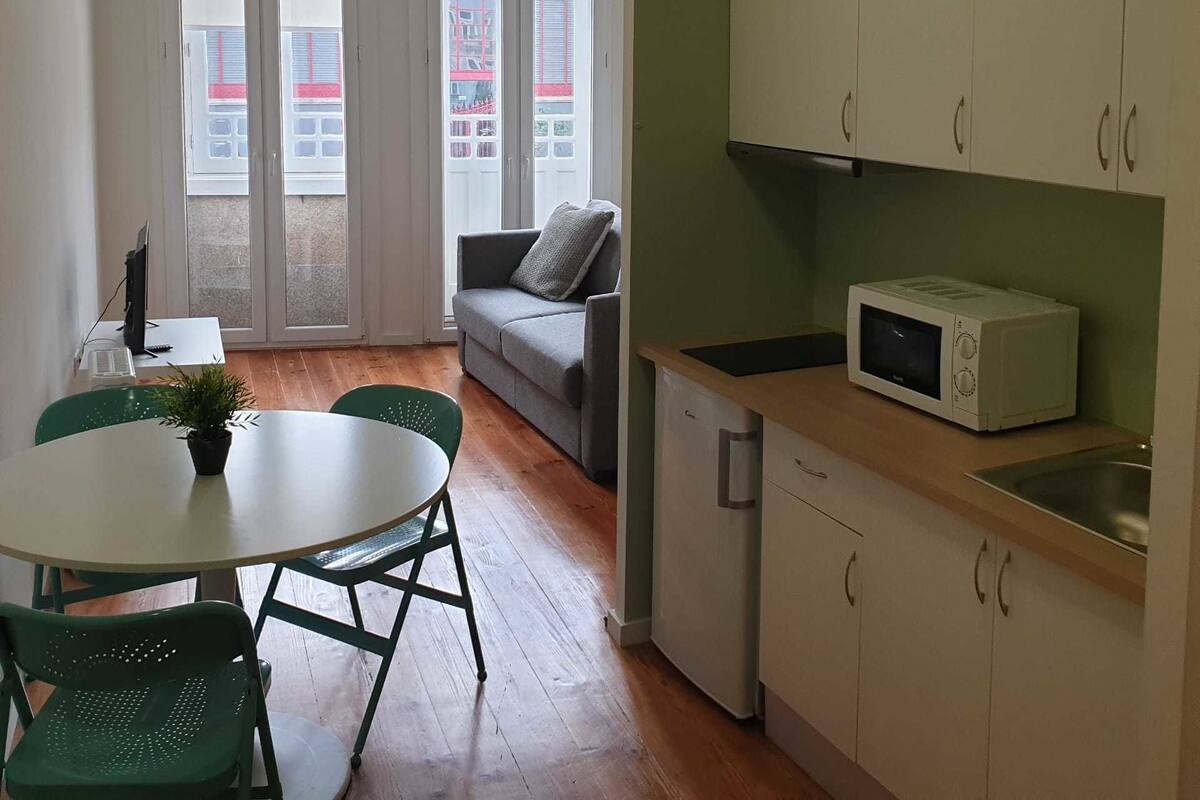 Espaço compacto com área de refeições, cozinha compacta e sofá próximo a uma porta de correr de vidro.