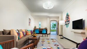 Sala de estar com sofá, cadeiras, mesa de centro e televisão. Ao fundo, há uma área de jantar com mesa e cadeiras.