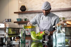 Um chef preparando uma salada com um frasco de molho.