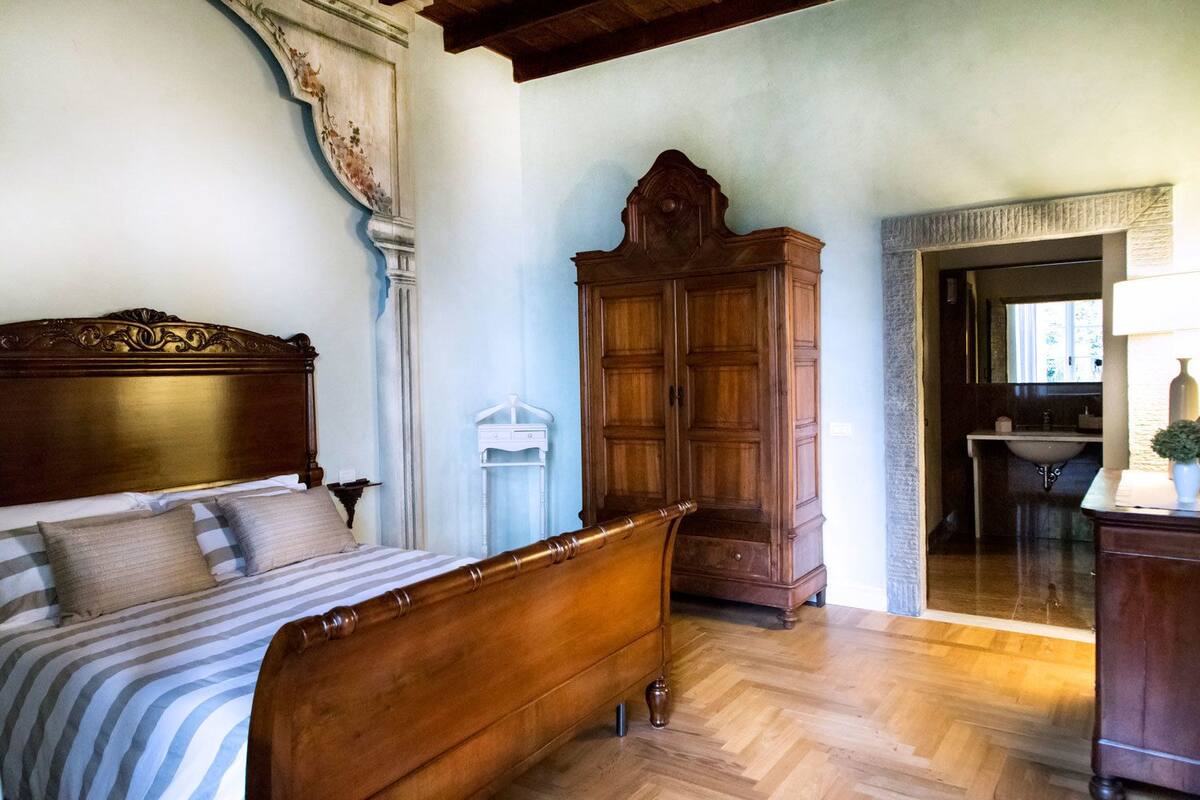 Quarto com cama de madeira, guarda-roupa e banheiro visível através de uma porta aberta.