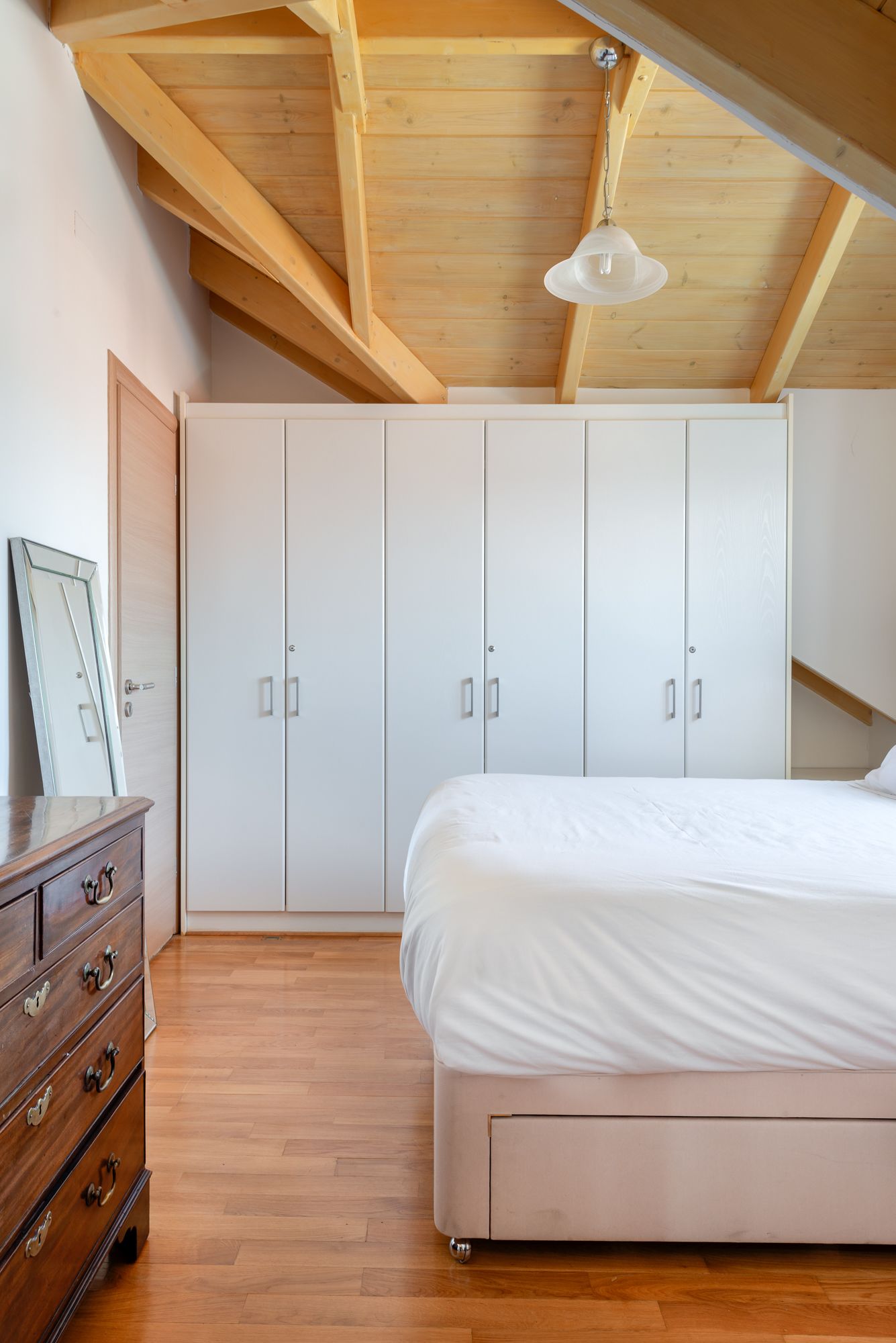 Quarto com teto de madeira, uma cama, cômoda e guarda-roupa.