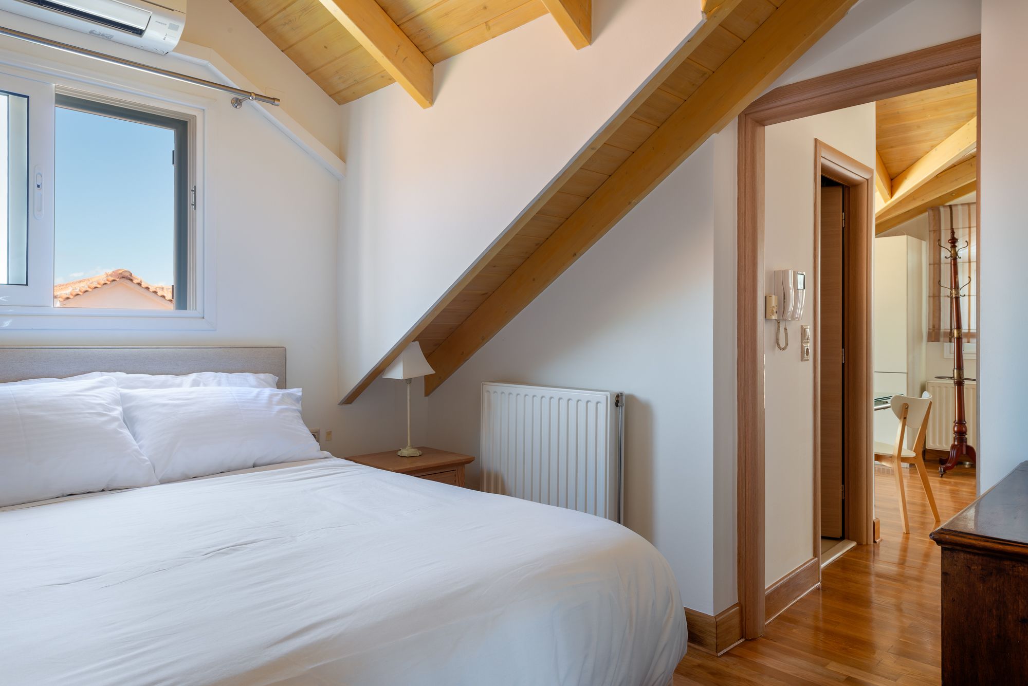 Quarto com cama, janela, radiador e teto de madeira.