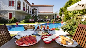 Uma mesa de jantar com diversos alimentos e uma piscina ao fundo.