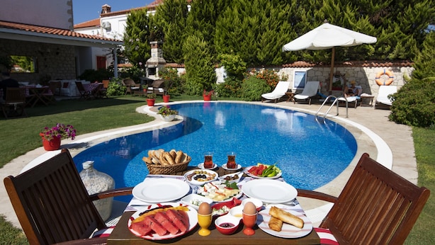 Disposição para café da manhã à beira da piscina, com mesa, cadeiras e diversas opções de comida.