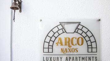 Placa para 'ARCO NAXOS LUXURY APARTMENTS' com um sino e um design de arco de tijolos.
