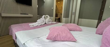 Quarto de hotel moderno com uma cama grande, televisão de tela plana na parede e banheiro visível através de uma porta aberta.