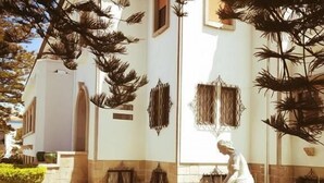 Um edifício com uma estátua no jardim, rodeado por árvores e plantas.
