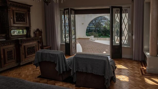 Quarto com piso de madeira, duas poltronas estofadas, um armário com espelho e vista para um caminho de tijolos que leva para o exterior.