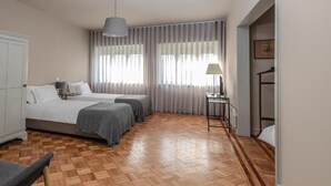 Quarto de hotel com duas camas, piso de parquet em madeira, uma secretária com abajur e um guarda-roupa.