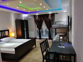 Quarto de hotel com beliche, uma cama de solteiro, escrivaninha com cadeira e televisão na parede.