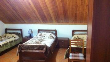 Um quarto pequeno e acolhedor com duas camas de solteiro, uma cadeira e uma mesa de cabeceira com abajur.