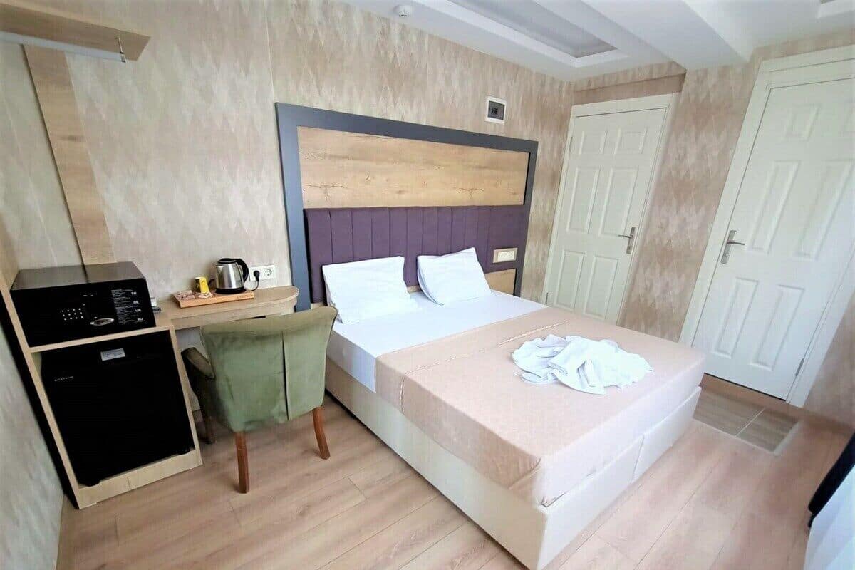 Um quarto com cama, escrivaninha com computador, máquina de café e guarda-roupa.
